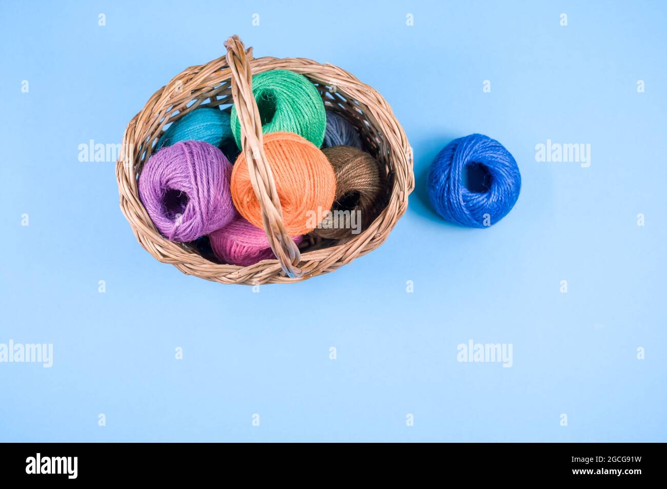 A pile of colorful textile balls of wool in a wicker basket on blue ...