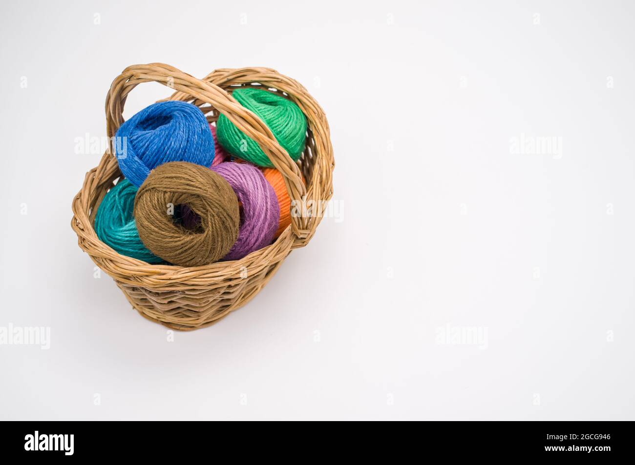 A pile of colorful textile balls of wool in a wicker basket on white ...