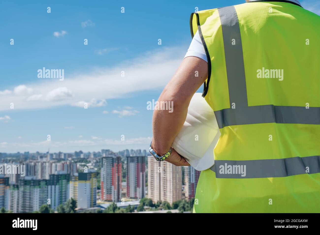 Man holds white hard hat in his hand on the roof of building under ...