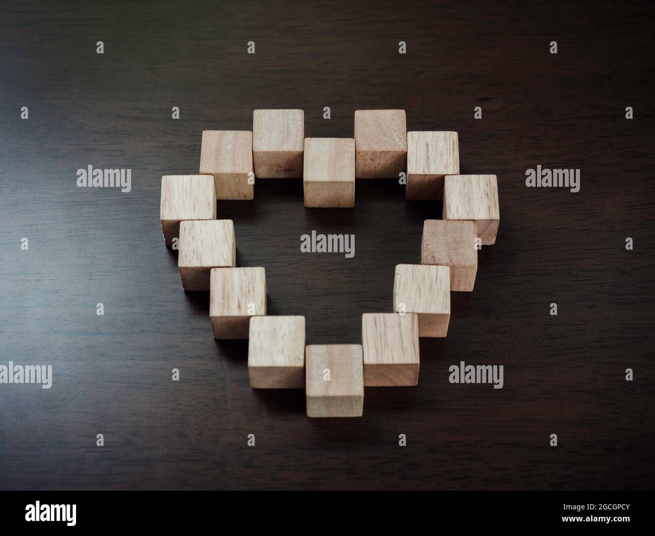 Wooden blocks arranged in heart shape on dark wood background, top view ...