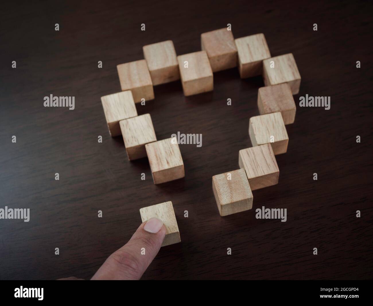 Human finger pushing on Wooden blocks, arranging in heart shape on dark ...