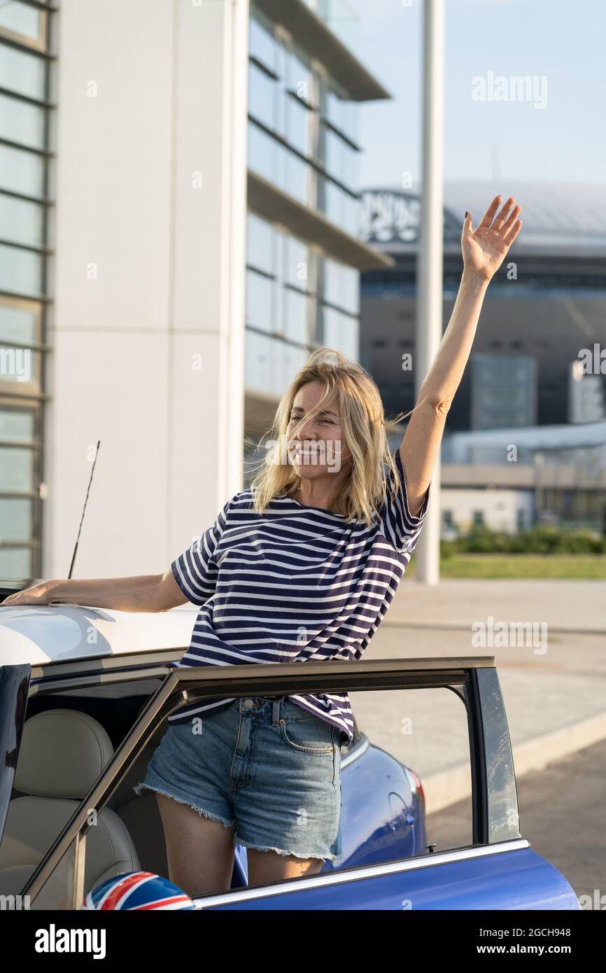 Carefree female driver look out of car wave hand happy to go on road ...