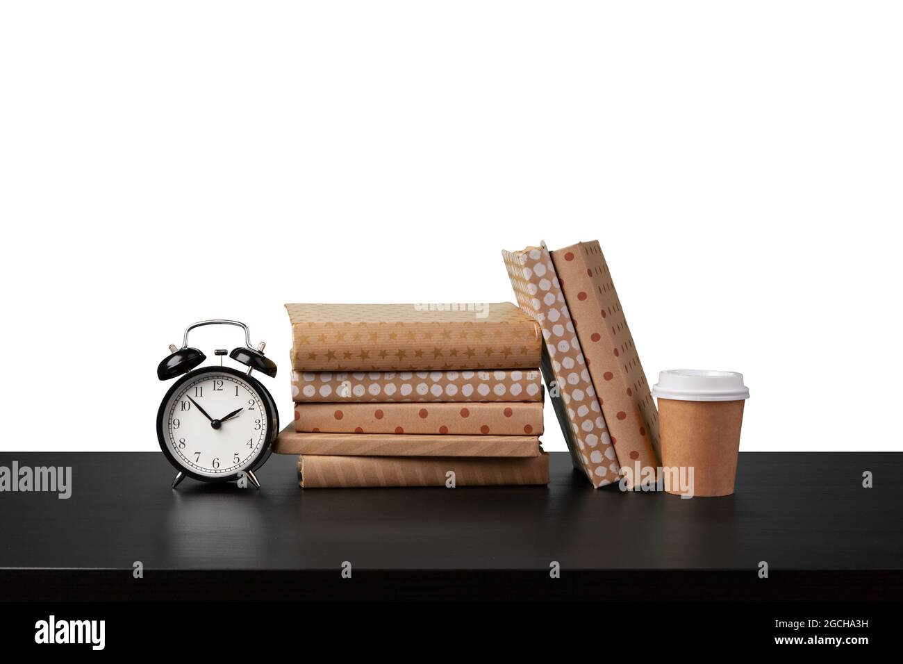 Alarm clock, stack of books and cup on tabletop against white ...