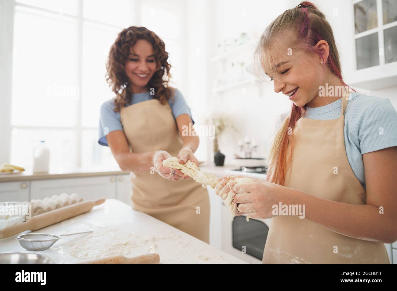 Teen girl helping her mom to cook dough in their kitchen at home Stock ...