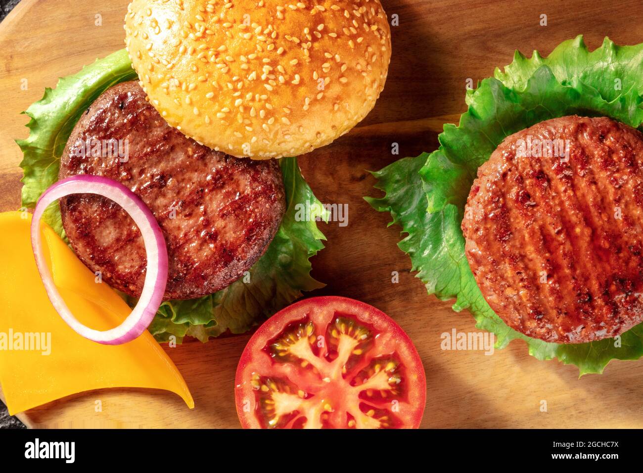 Burger ingredients close-up on a wooden board. Beef patty, sesame bun ...