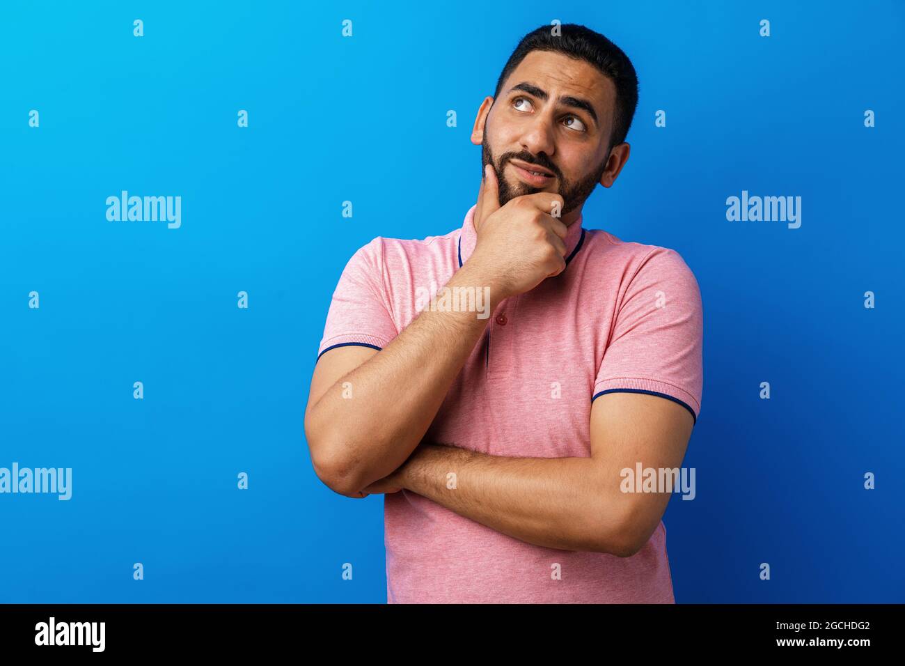 Pensive young arab man thinking and looking up against blue background ...