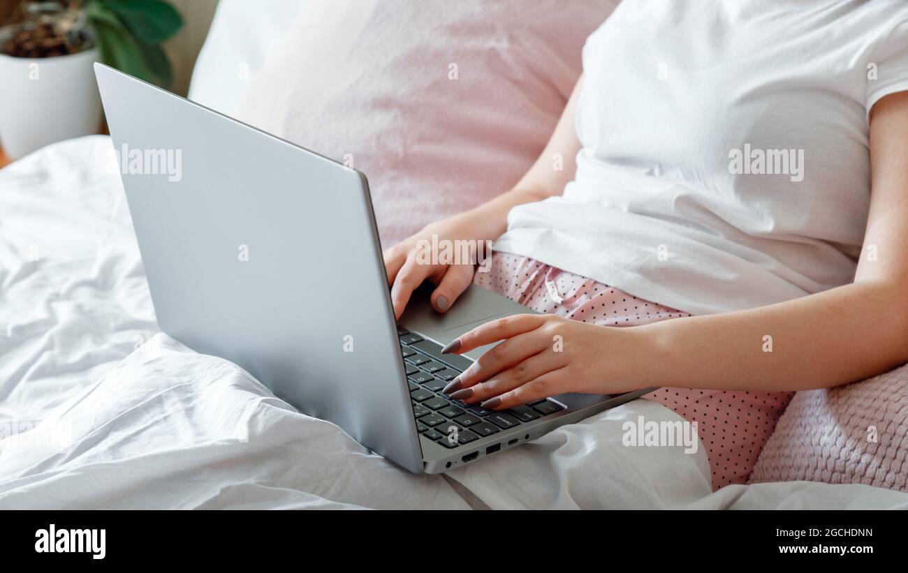 Female hands typing on laptop keyboard while lying in bed. Woman work ...