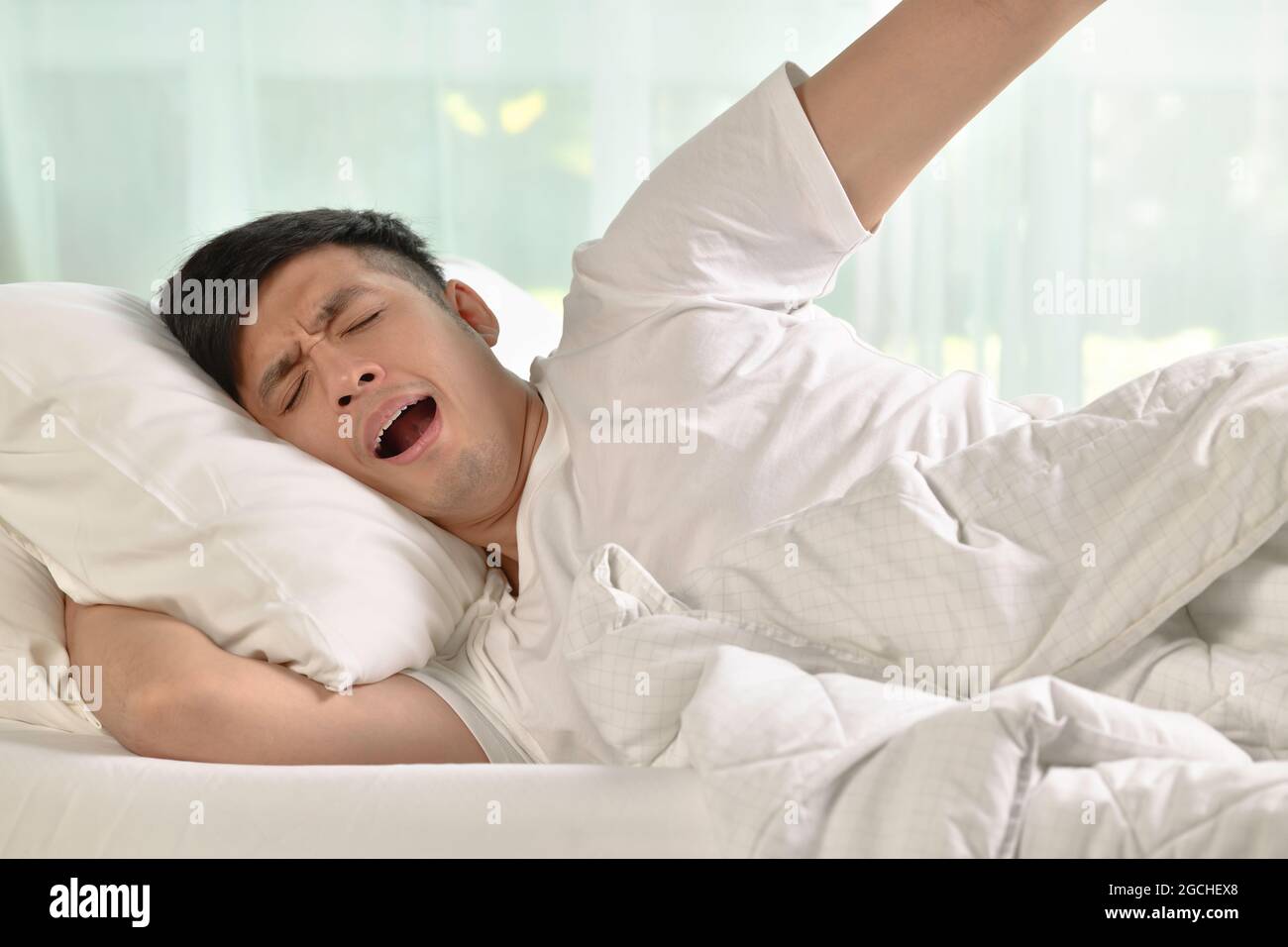 Young asian man yawning and stretching while waking up in the morning Stock Photo - Alamy