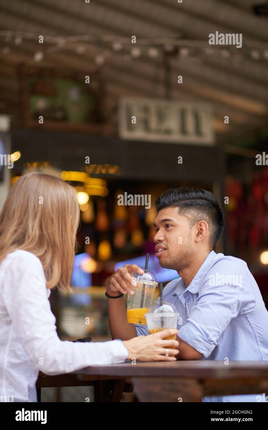 Pretty smiling young woman enjoying refreshing drink and conversation ...