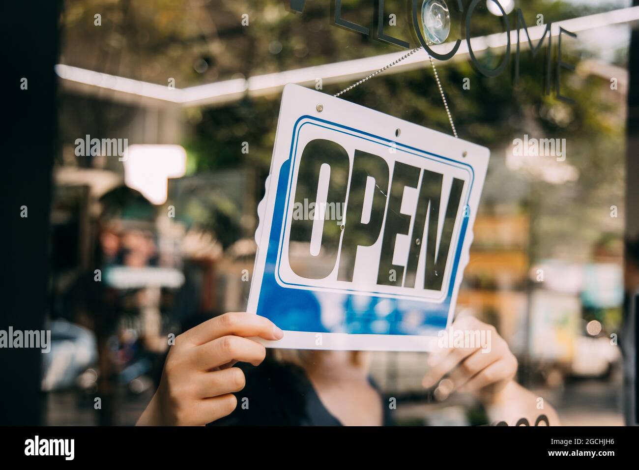 Young Asian woman hanging open sign by glass window. Female shop owner ...