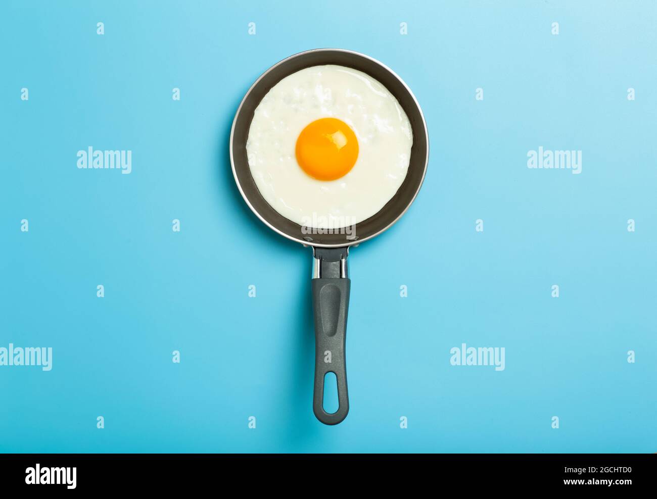 Fried egg is minimal. Fried egg in a frying pan on an empty blue ...