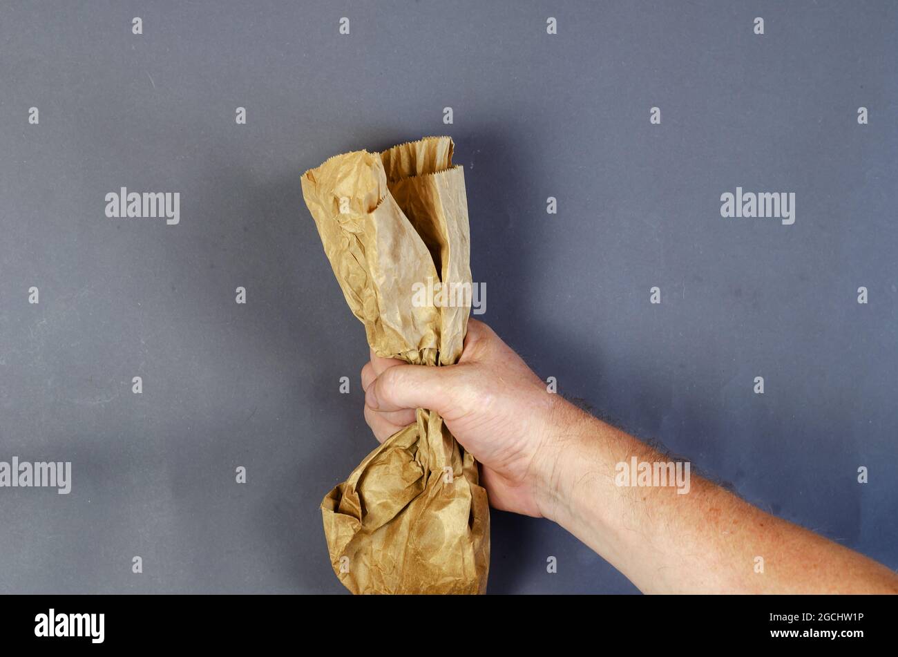 Man holding a dirty brown paper bag on a gray background. Hand crumples ...