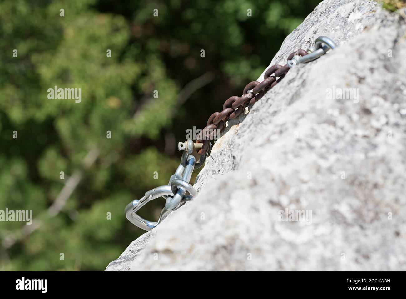 Climbing carabiner on a rusty steel chain attached to rock above ...