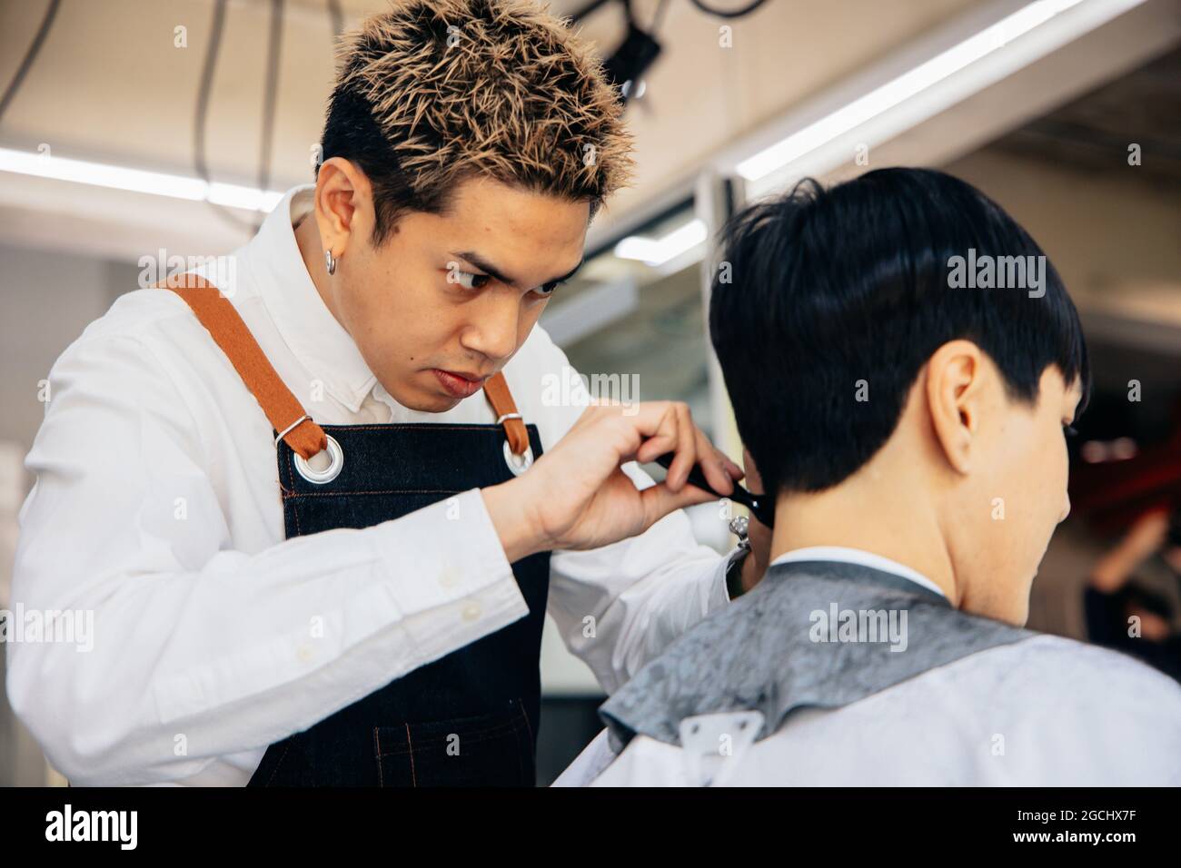 Happy young Asian male hairdresser smiling wearing apron in modern ...
