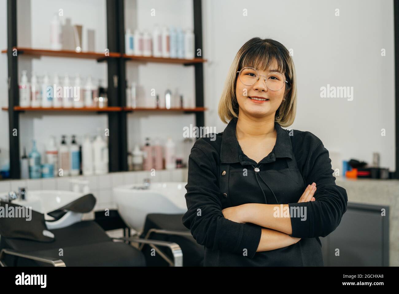 Portrait of happy successful young Asian salon owner standing wearing ...
