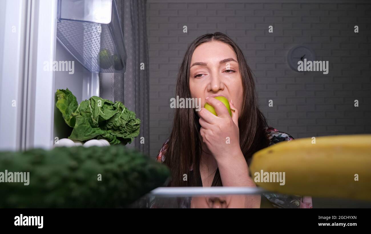 Thoughtful woman looks for snacks and chooses green apple Stock Photo ...