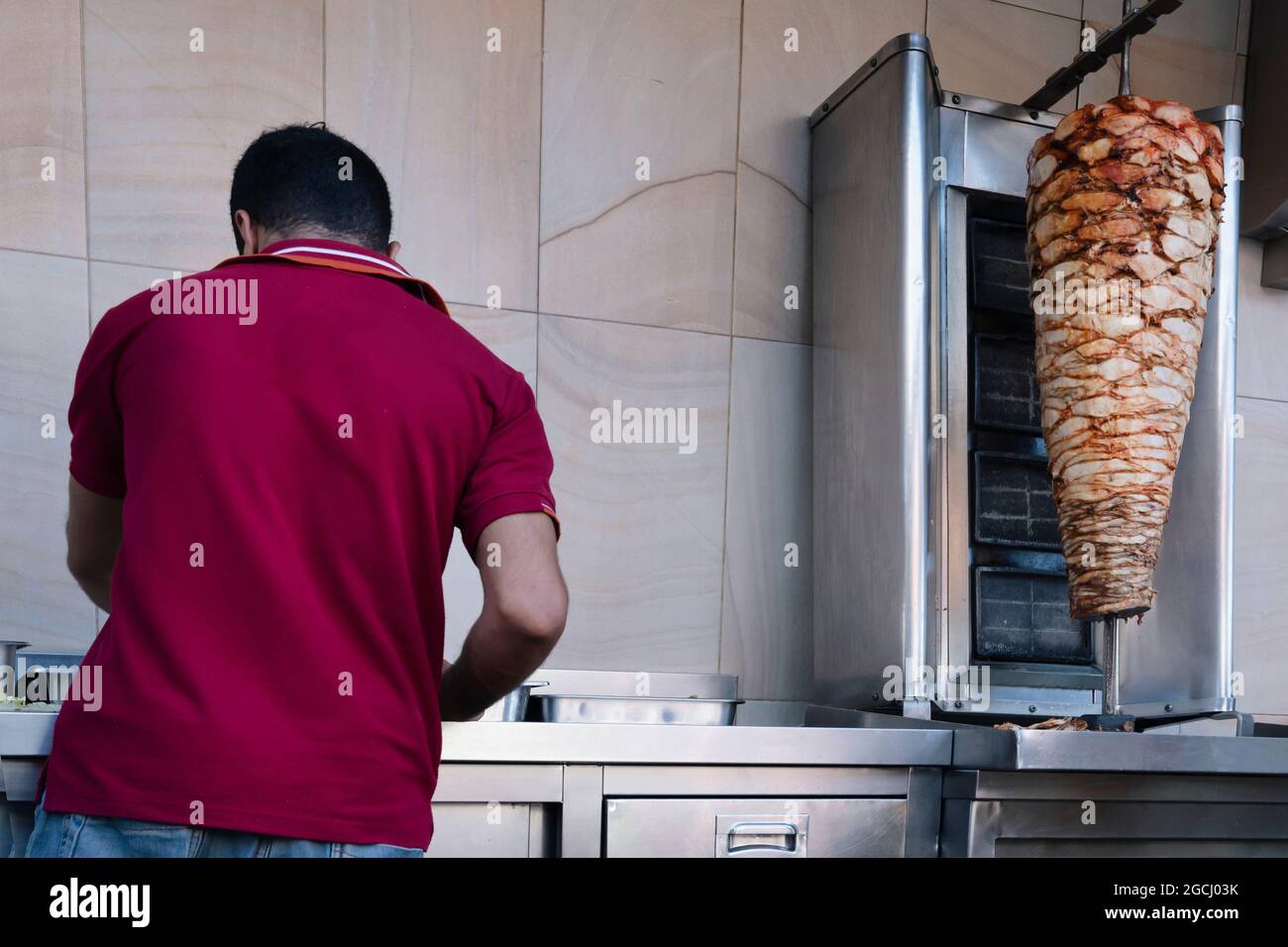 an Arab cook prepares shawarma, cuts meat. standing with his back to ...