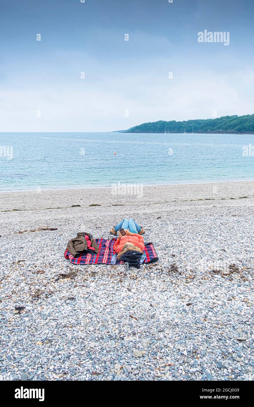 A holidaymaker relaxing on the shingle beach at Polgwidden Cove Trebah ...
