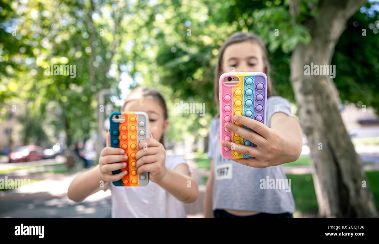 Little girls with phones in a case with pimples pop it, a trendy anti ...