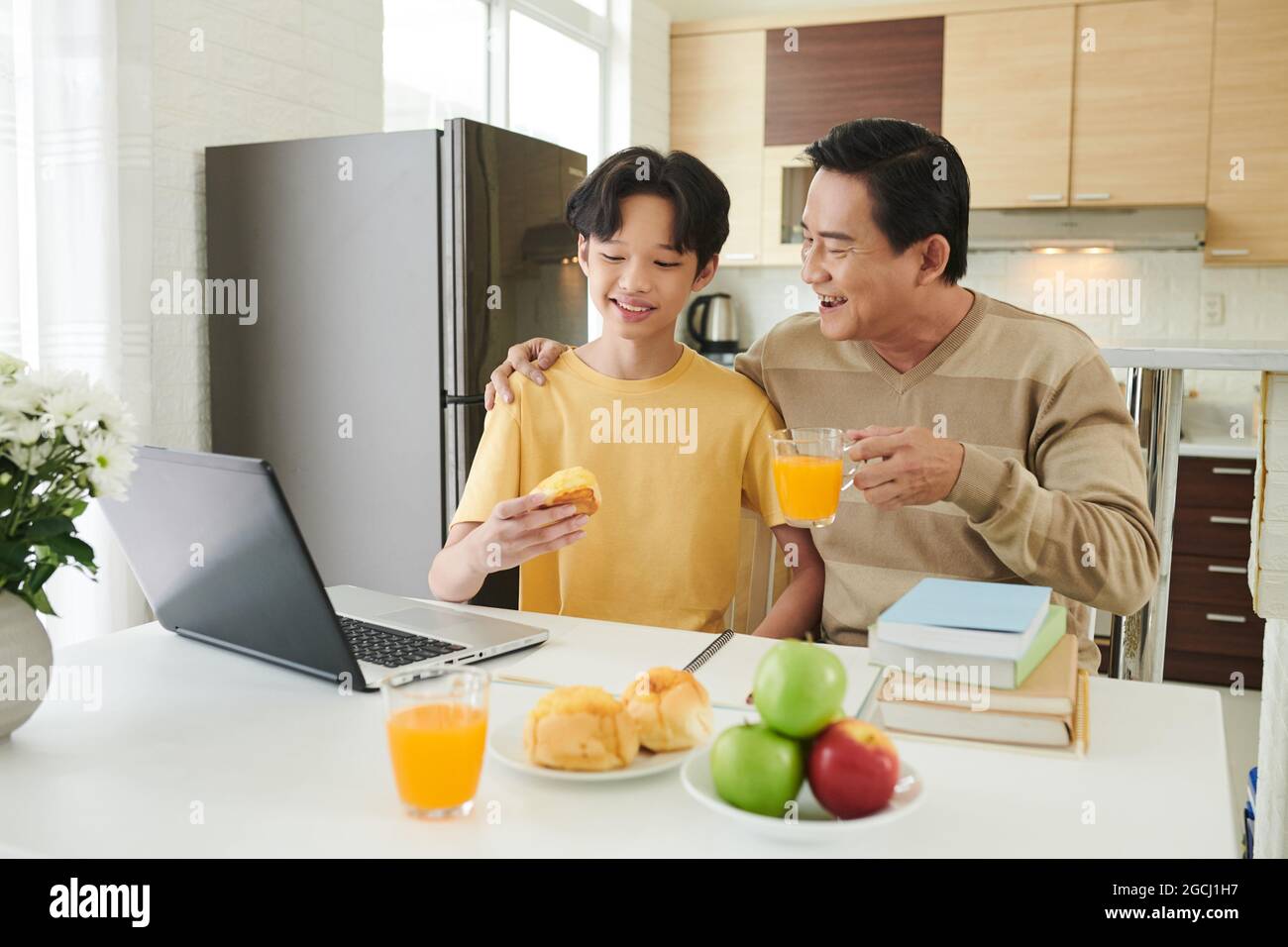 Happy father and son enjoying fresh buns with orange juice and ...