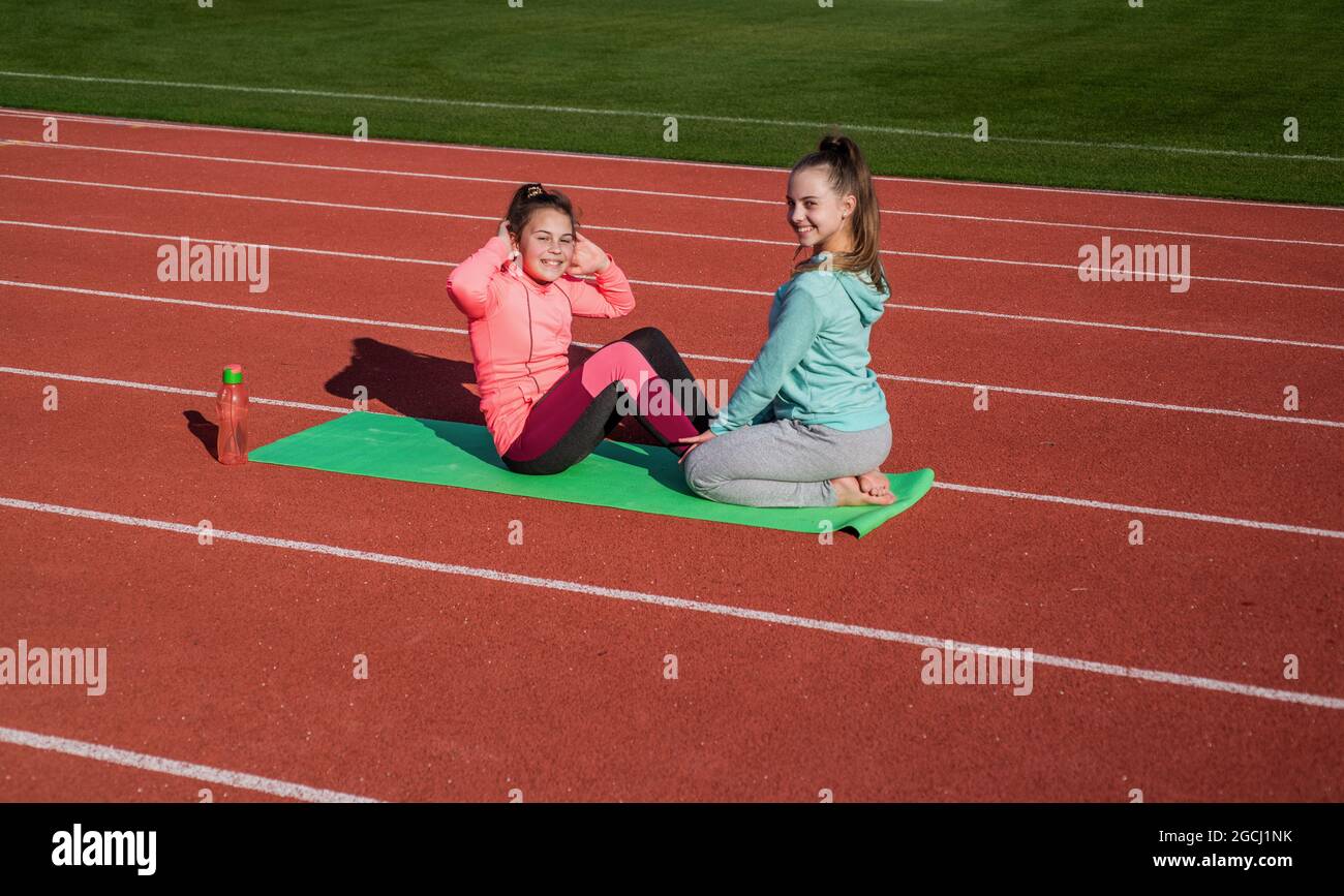 Happy fit teenage girls do situps physical training on athletics track ...