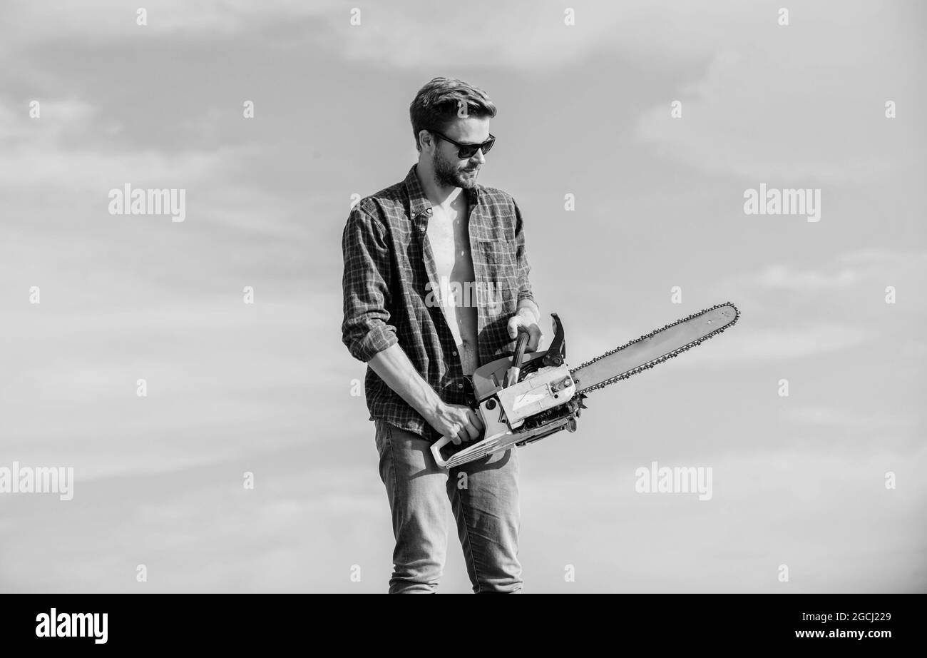 Handsome man with chainsaw blue sky background. Gardener lumberjack ...