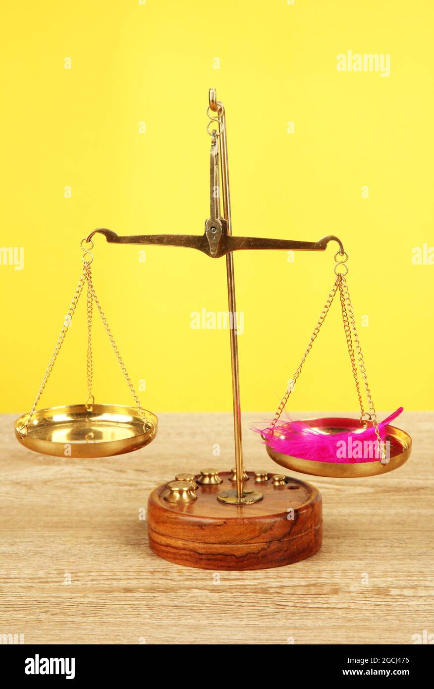 Balance scale with feather on table on yellow background Stock Photo ...