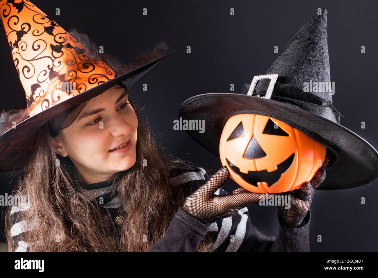 A woman in a witch costume in an orange hat holds a pumpkin lantern ...
