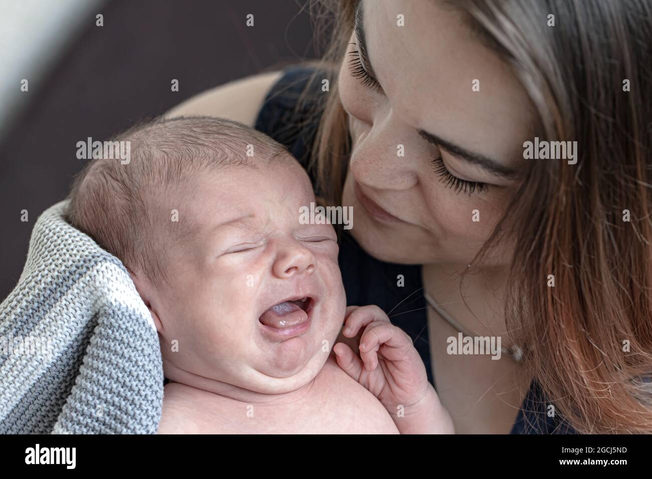 Young mother holds a crying newborn baby boy in her arms, close up ...