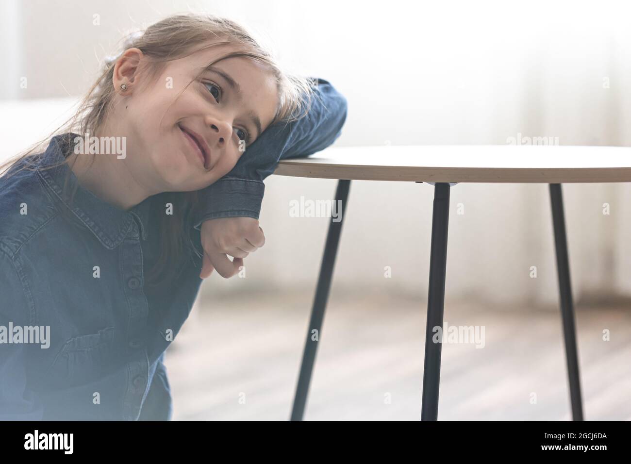 Cute little girl leaning on the table and looking into the distance ...