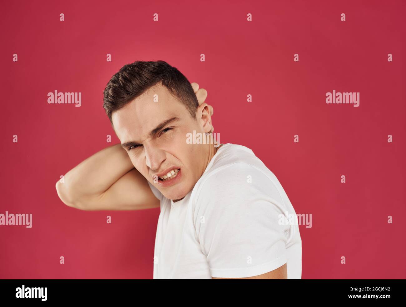 a man with an angry expression holds his hand behind his head white t ...