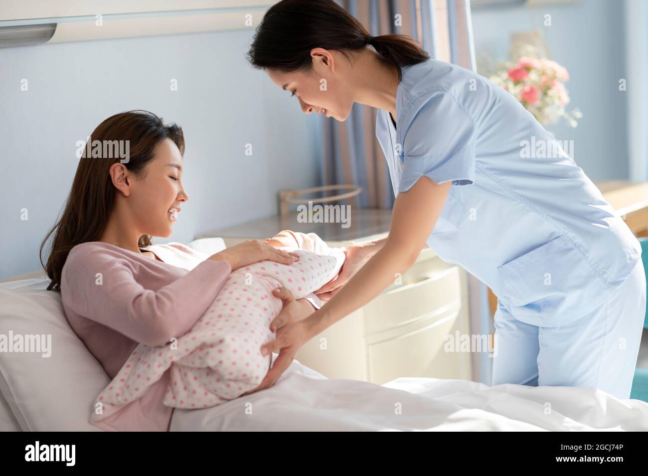 Female nurse handing newborn baby to mother in hospital ward Stock ...