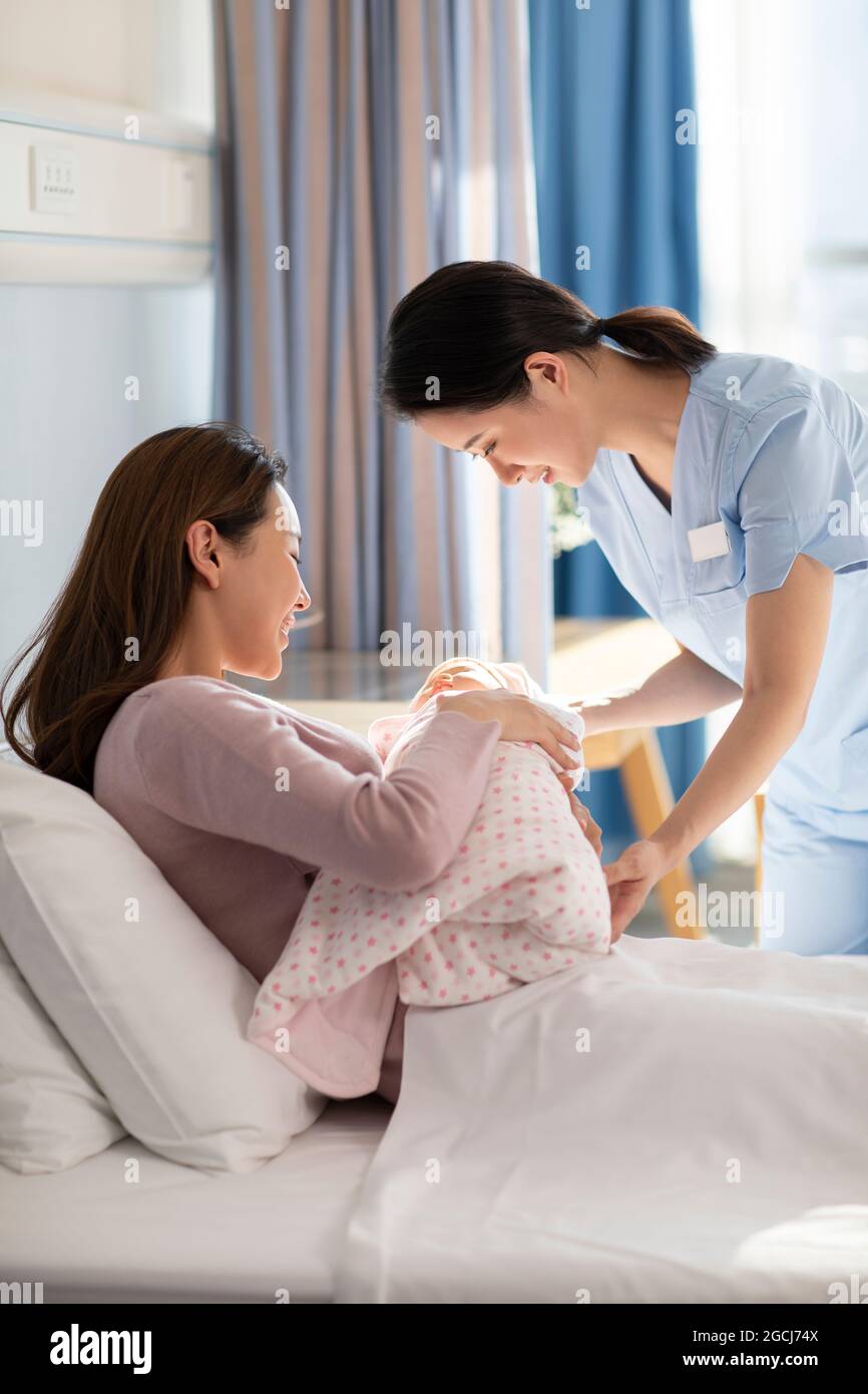 Female nurse handing newborn baby to mother in hospital ward Stock ...