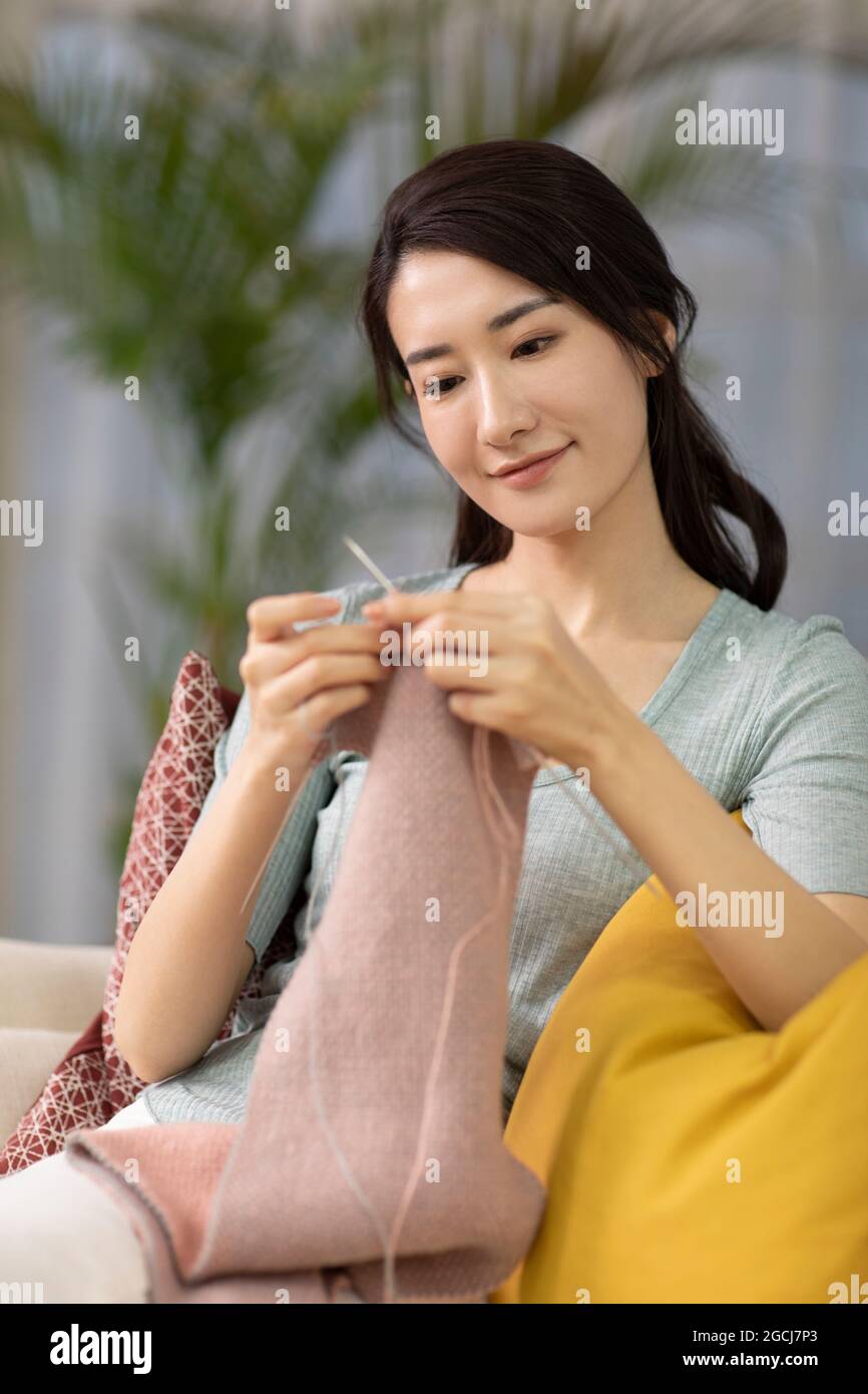 Happy young woman knitting in living room Stock Photo - Alamy