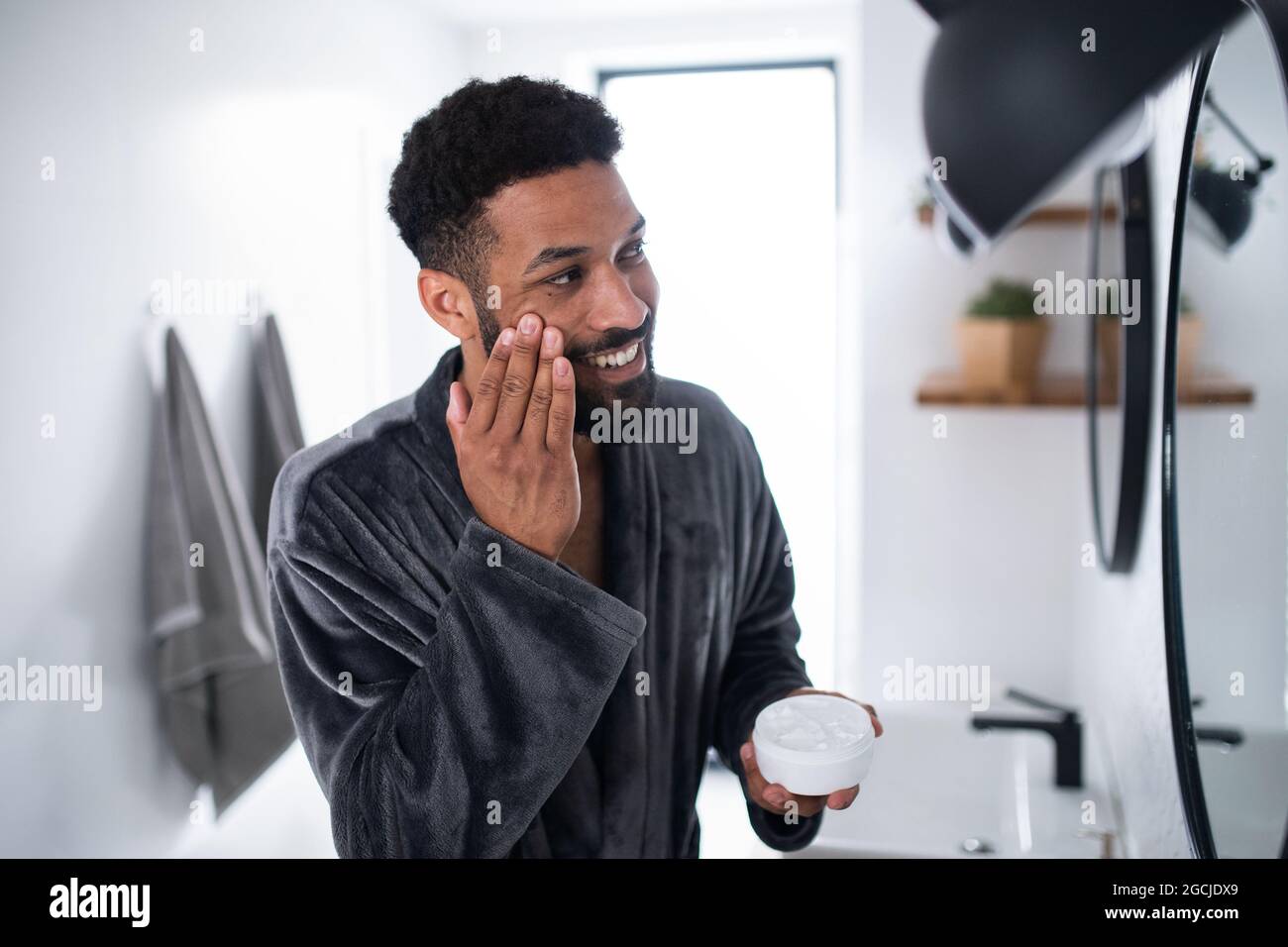 Young man applying cream on face indoors at home, morning or evening ...