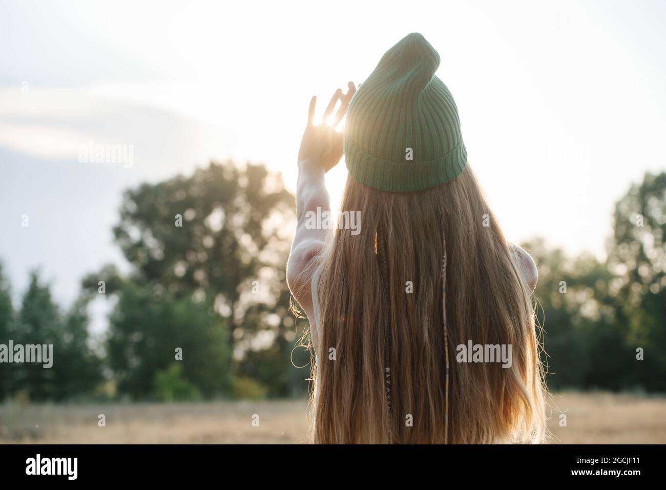Long-haired woman in a green watch cap blocking sun with her hands from ...