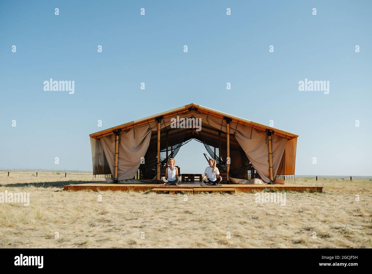 Long shot of two women meditating in easy pose on a doorstep of a huge ...