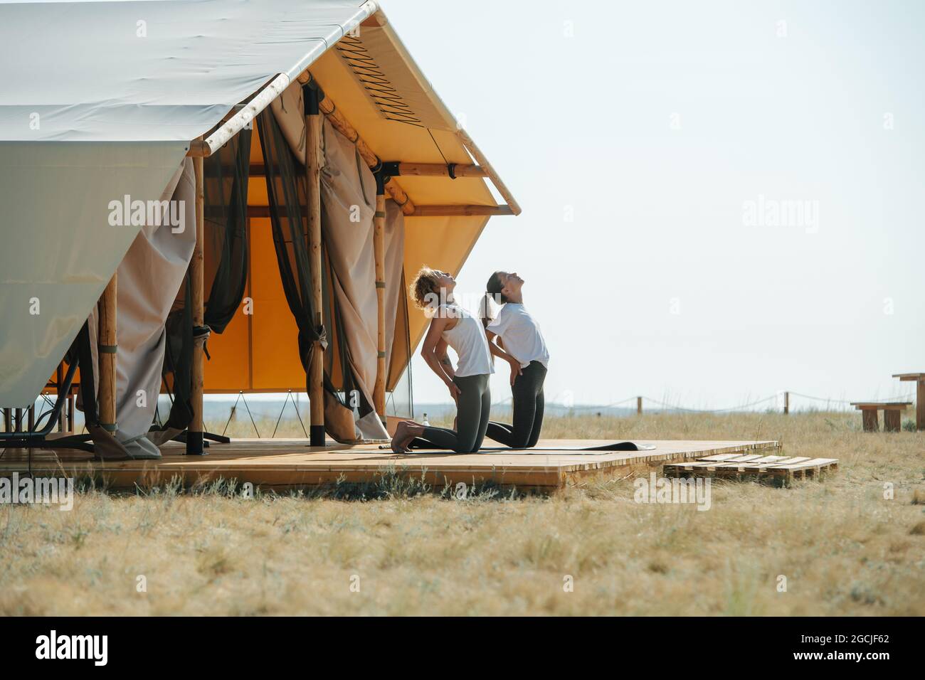 Side view of two women doing yoga, camel pose on a doorstep of a huge ...