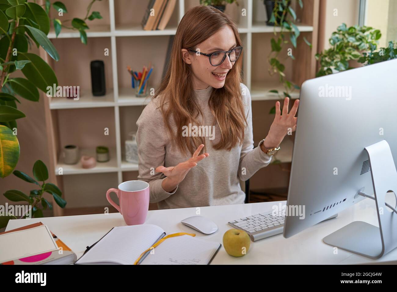 Happy lady looking at computer screen while gesturing with her hands ...
