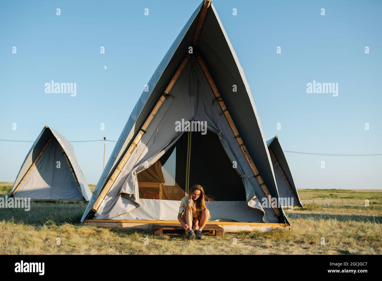 Woman sitting on a doorstep of a huge wooden pole tent, lacing her ...