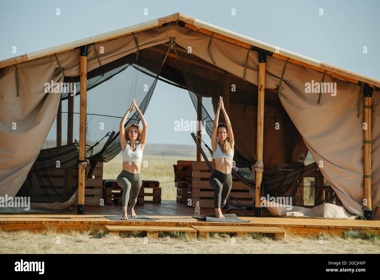 Women doing yoga, holding warrior asana on a doorstep of a huge wooden ...