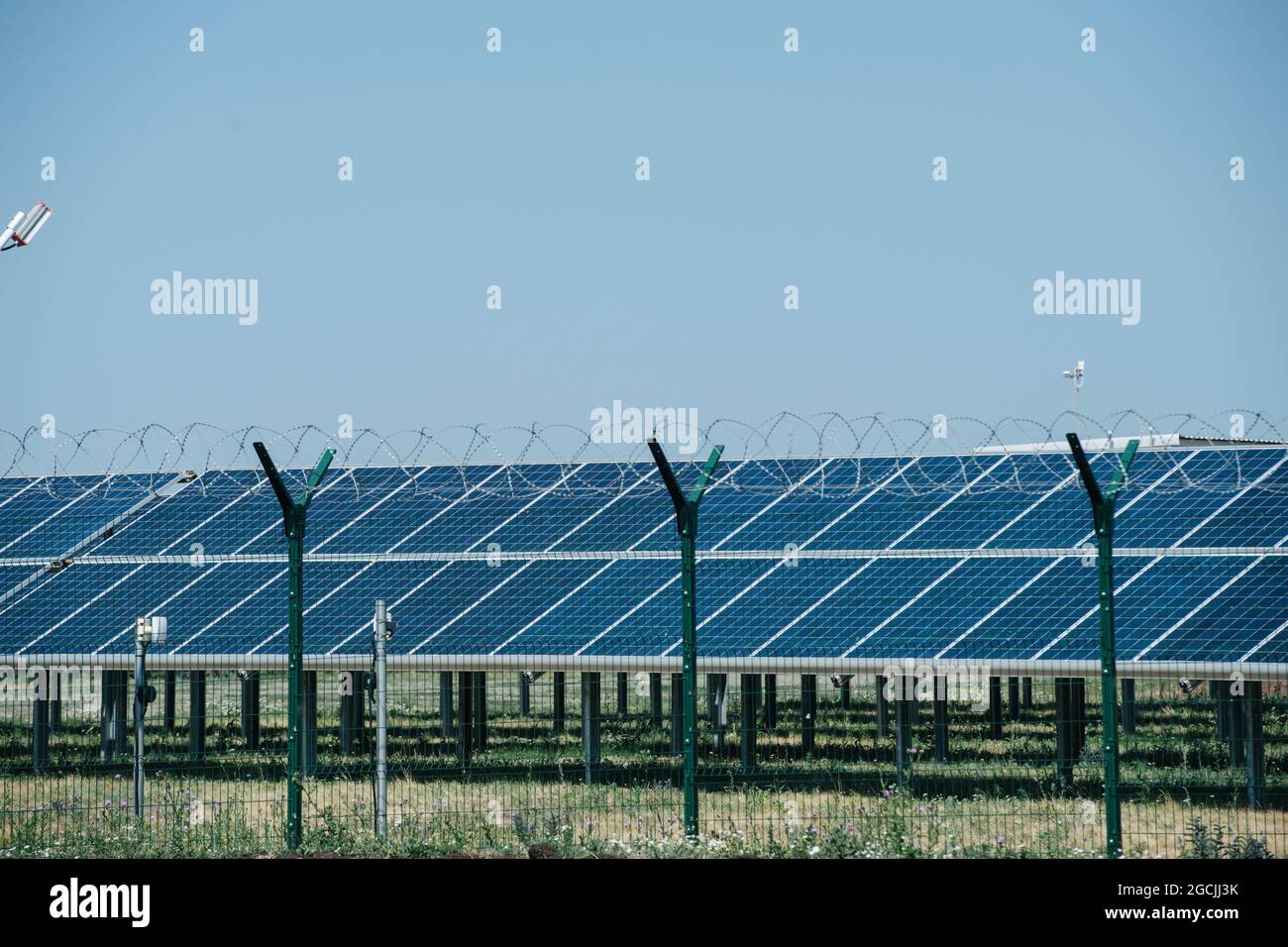 Small solar farm behind a fence. Front view. Clear blue sky over them ...