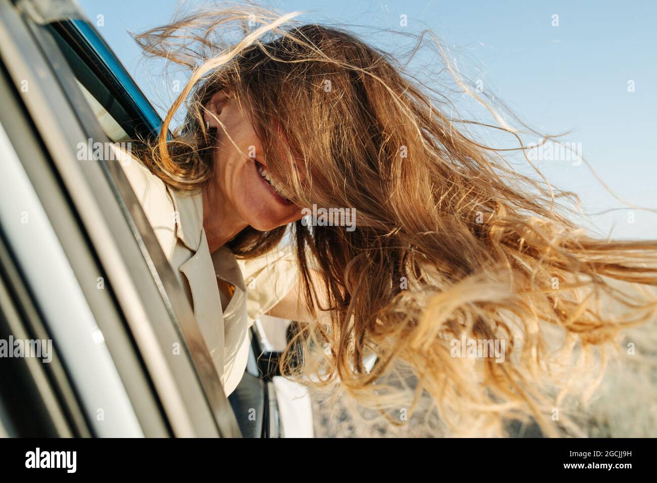 Funny cheerful woman sticking out of car window, hair getting in her ...