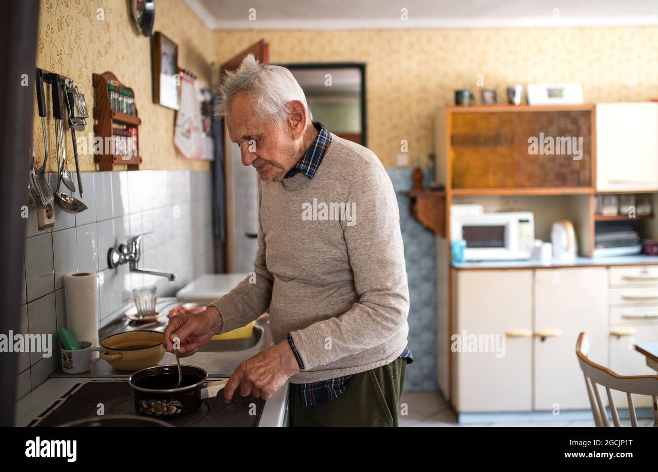 Portrait of elderly man cooking on stove indoors at home, stirring ...