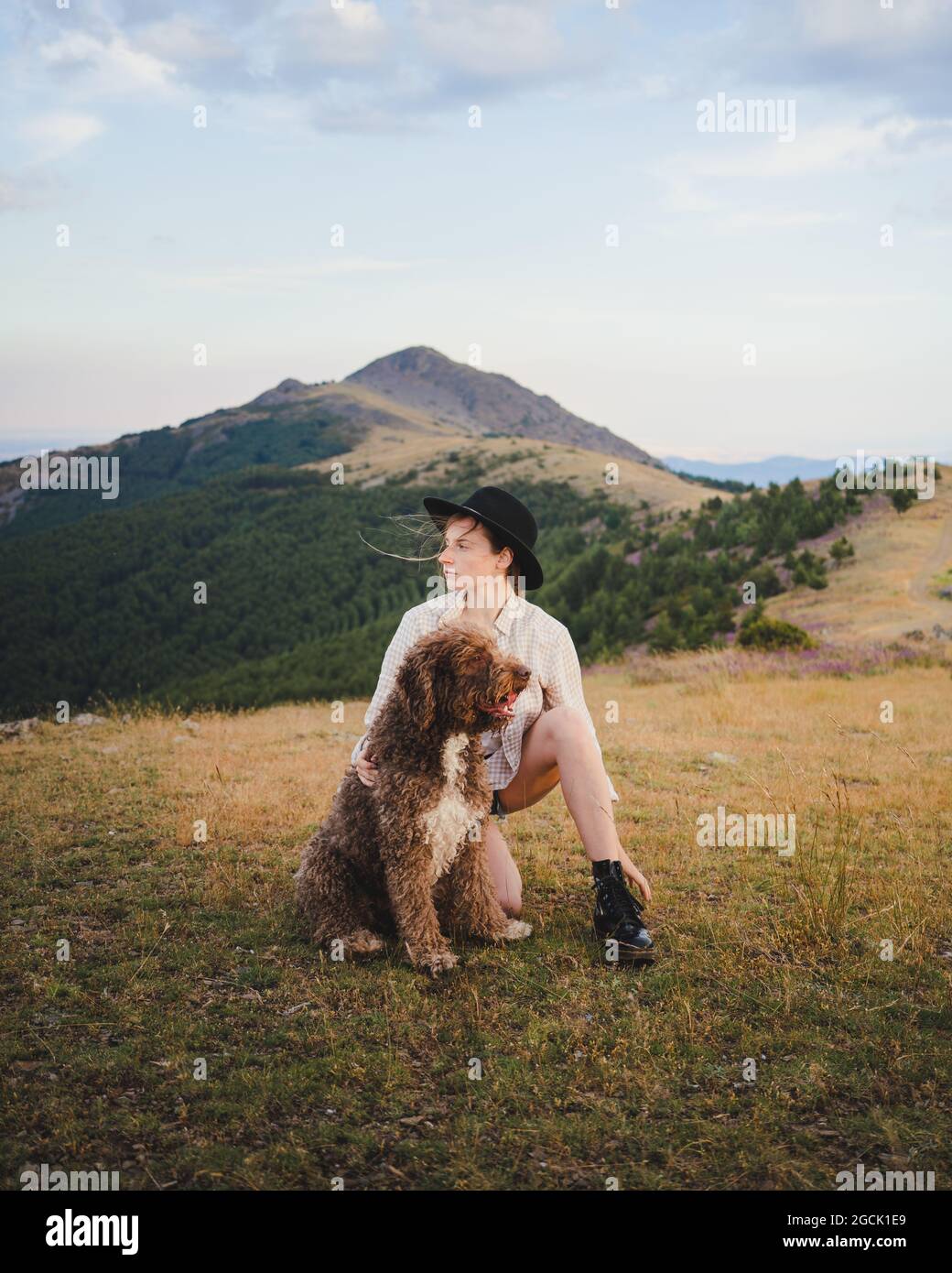 Female owner with obedient Labradoodle dog sitting in mountains looking ...