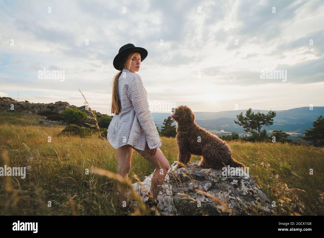 Side view of female owner with obedient Labradoodle dog sitting on rock ...