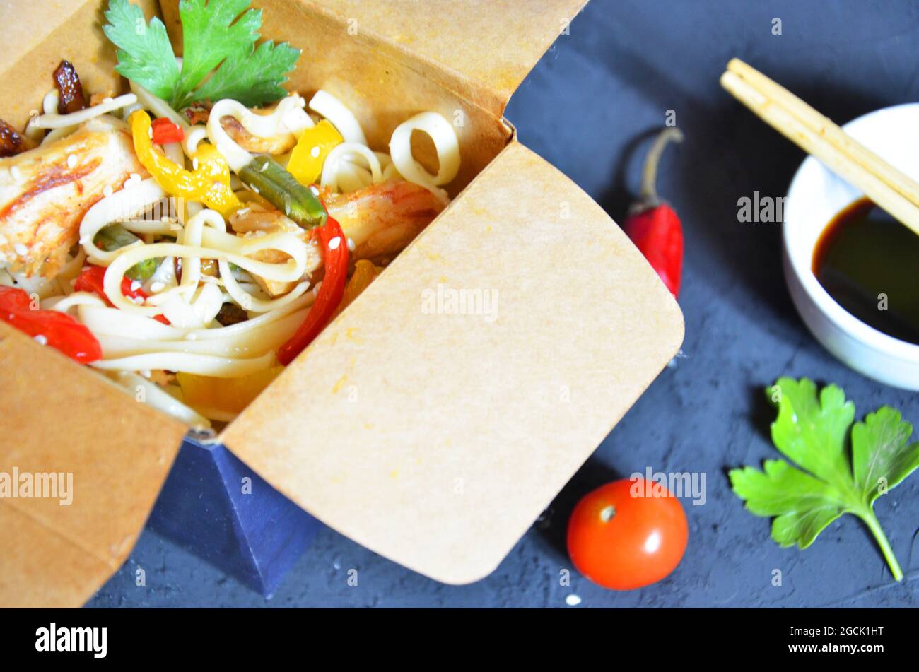 Noodles with pork and vegetables in take-out box on wooden table ...