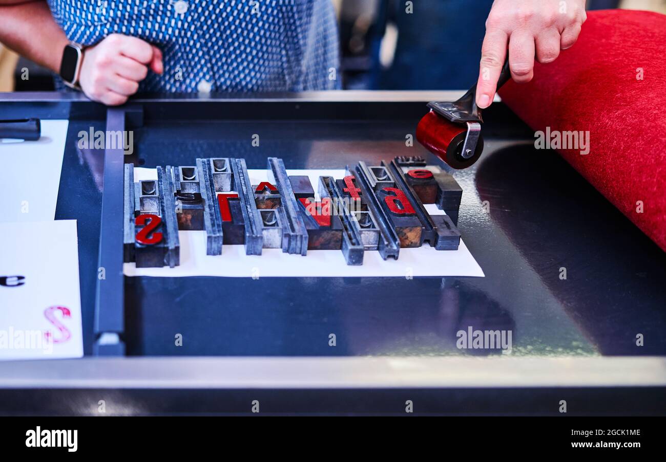 Crop unrecognizable male worker painting letterpress font with roller ...