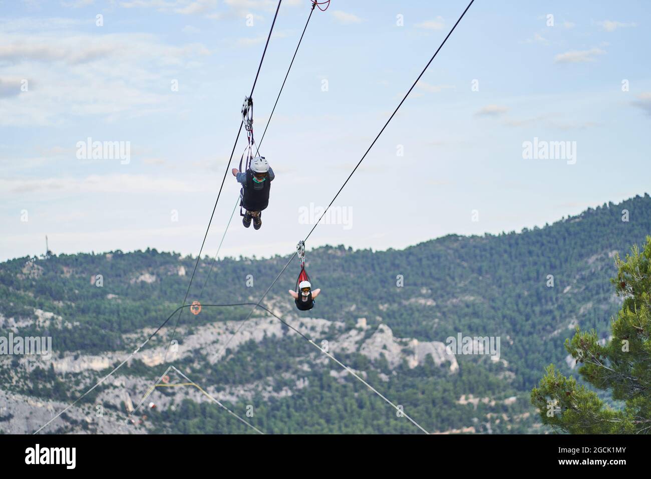 Anonymous brave people in safety equipment riding zip line over ...