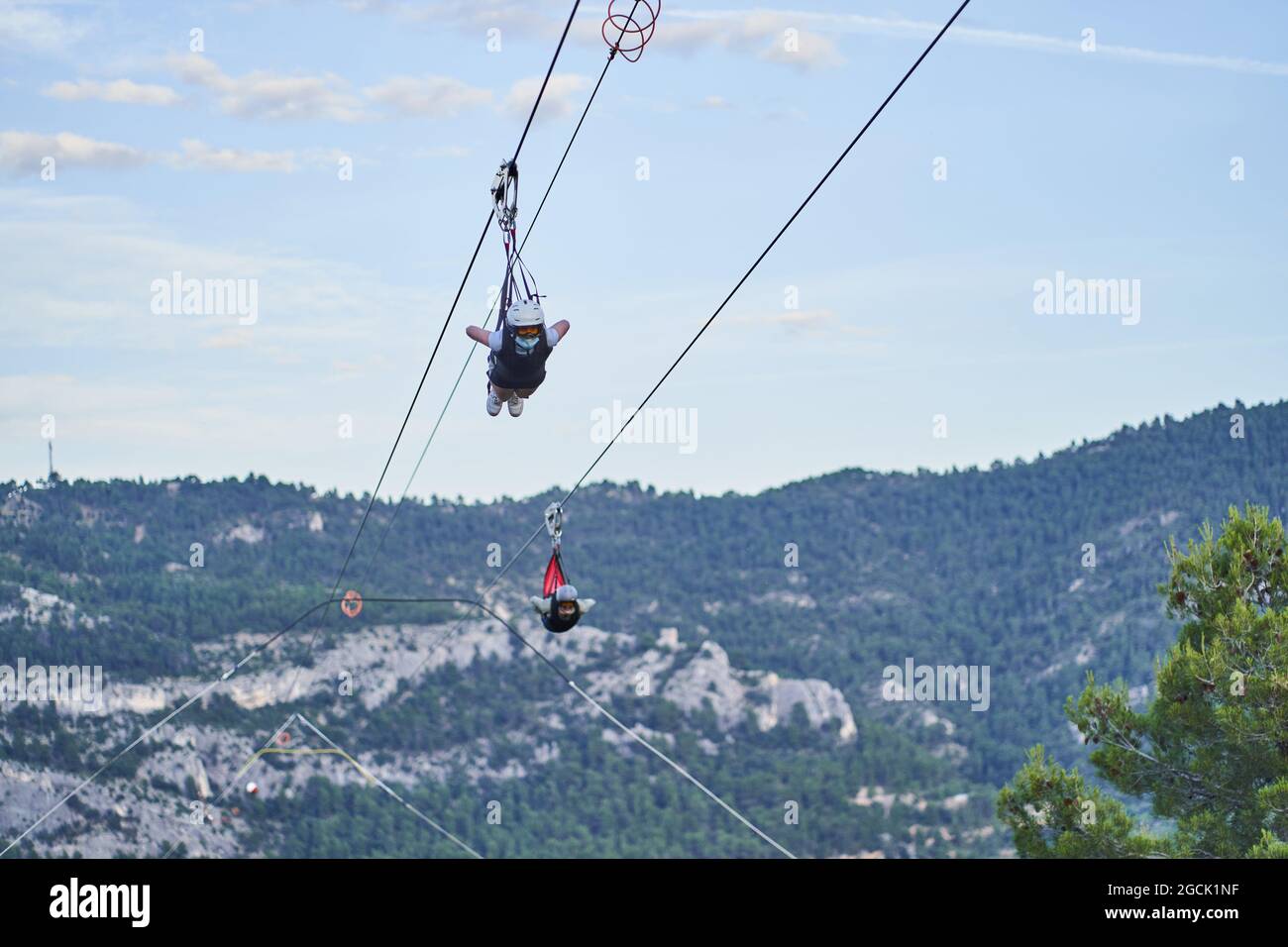 Anonymous brave people in safety equipment riding zip line over ...